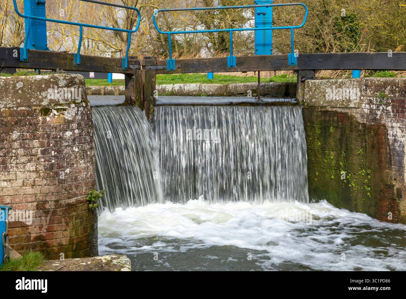 Water flowing over a canal lock weir with blue gates and brick walls ...