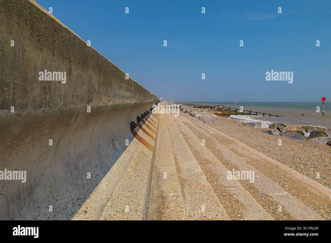 A concrete sea wall and stepped coastal defences along a shingle beach ...