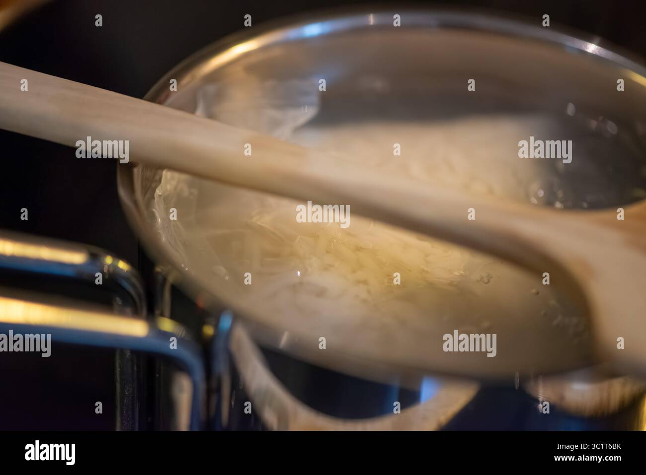 A candid kitchen scene showing a woman preparing rice, as boiling water ...