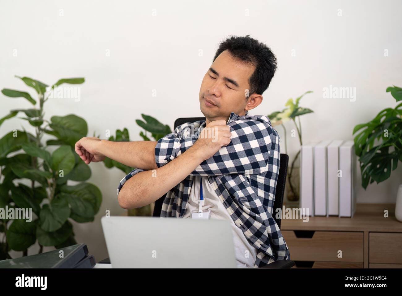 Health. Young man relieving tension by stretching at his desk Stock ...