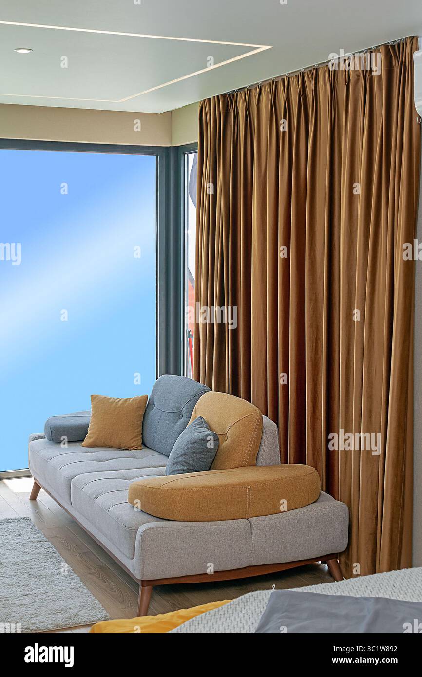 Modern sofa with pillows and hanging drapes inside home interior corner ...