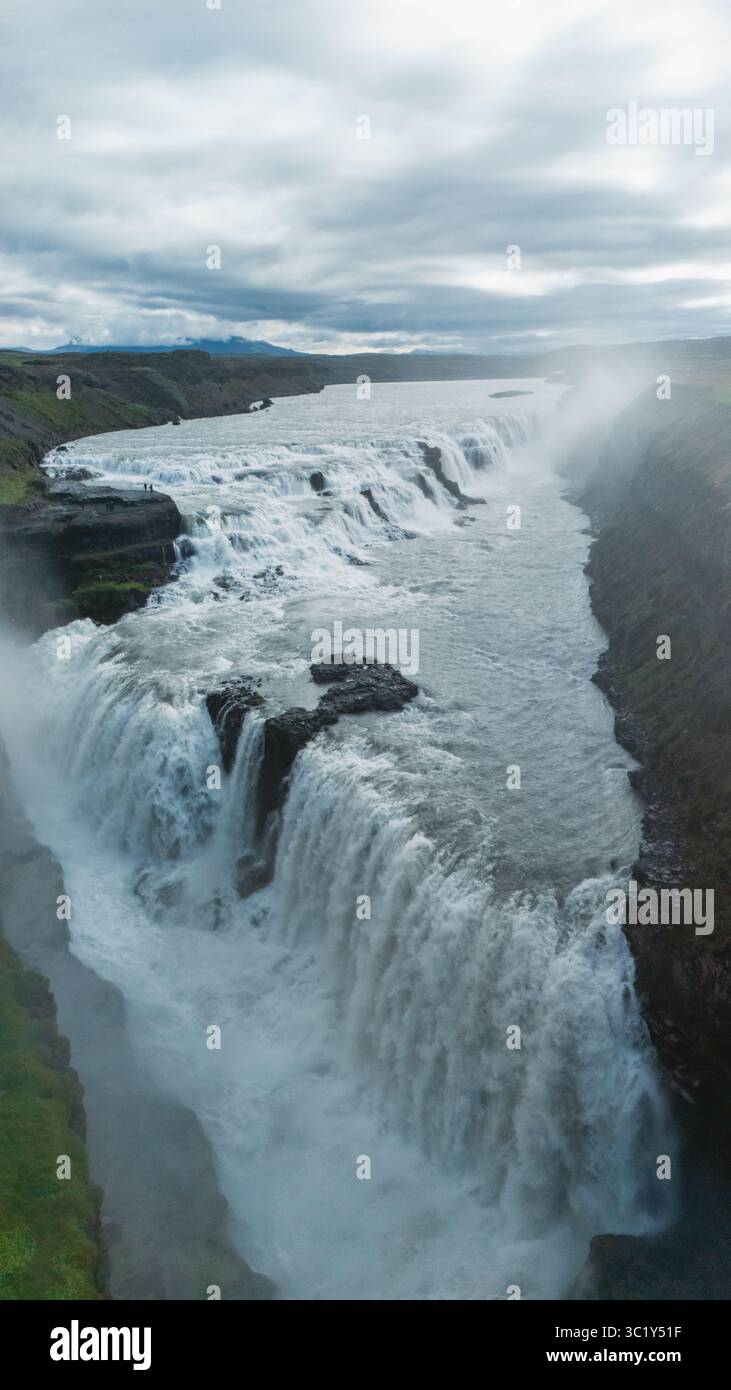 Witness the breathtaking sight of Gullfoss waterfalls flowing over rocky cliffs, surrounded by ...