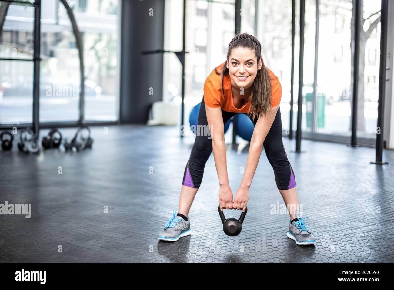 Woman lifting kettlebell in gym wearing workout clothes on rubber floor ...