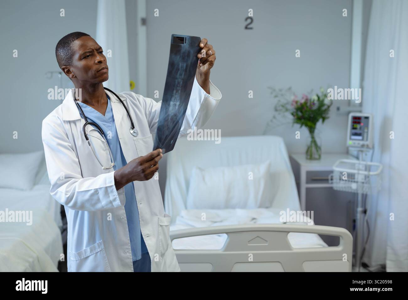 African American doctor with stethoscope holding X-ray film to light by ...
