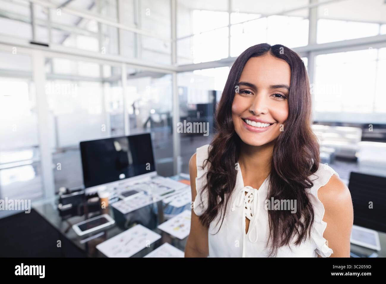 Female professional standing beside desk in open-plan office smiling ...