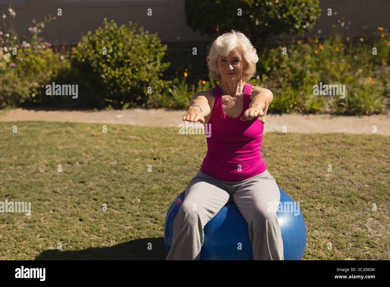 Senior woman balancing on blue stability ball on backyard lawn ...