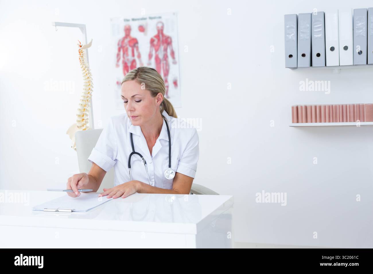 Medical professional writing notes on clipboard at consultation desk ...