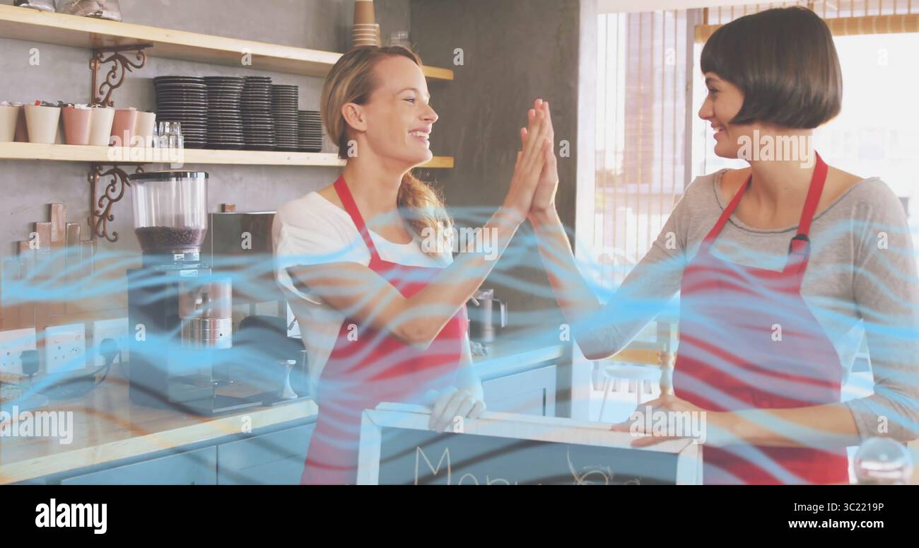 High-fiving two cafe staff wearing red aprons behind coffee shop ...