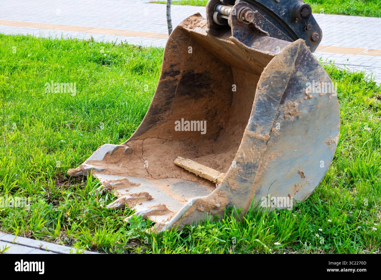 A large and robust excavator bucket is resting idle in the green grass ...
