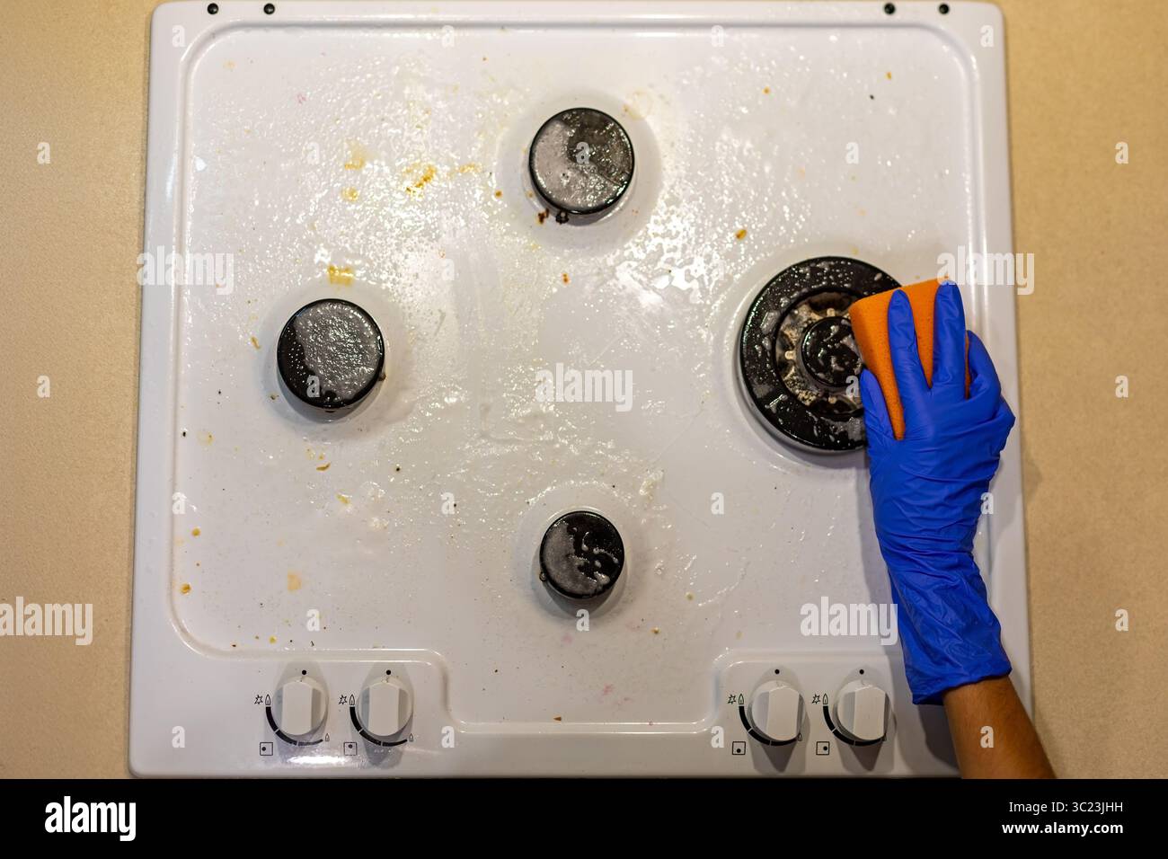 Cleaning dirty stove top with sponge and gloves. Person wearing blue ...