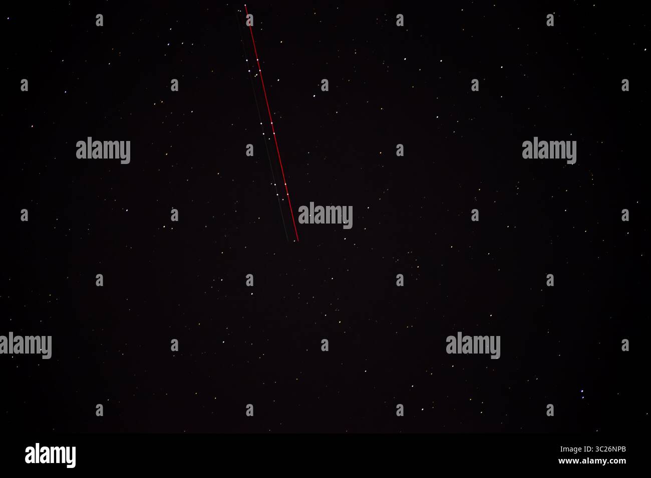 Long exposure image showing a red light trail across a starry night sky ...