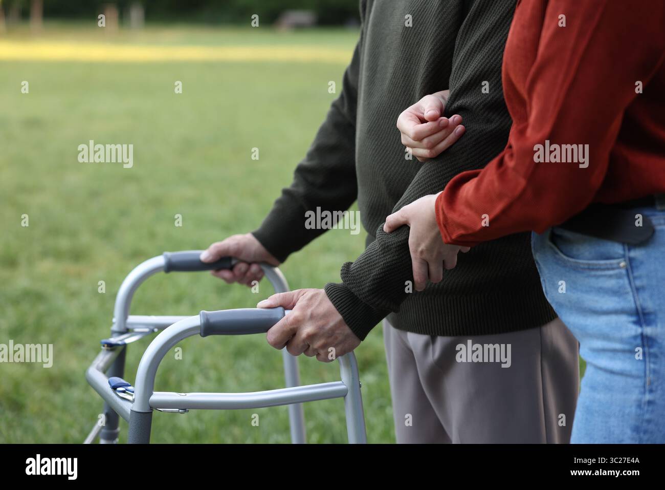 Caregiver supporting elderly man who using walking frame outdoors ...