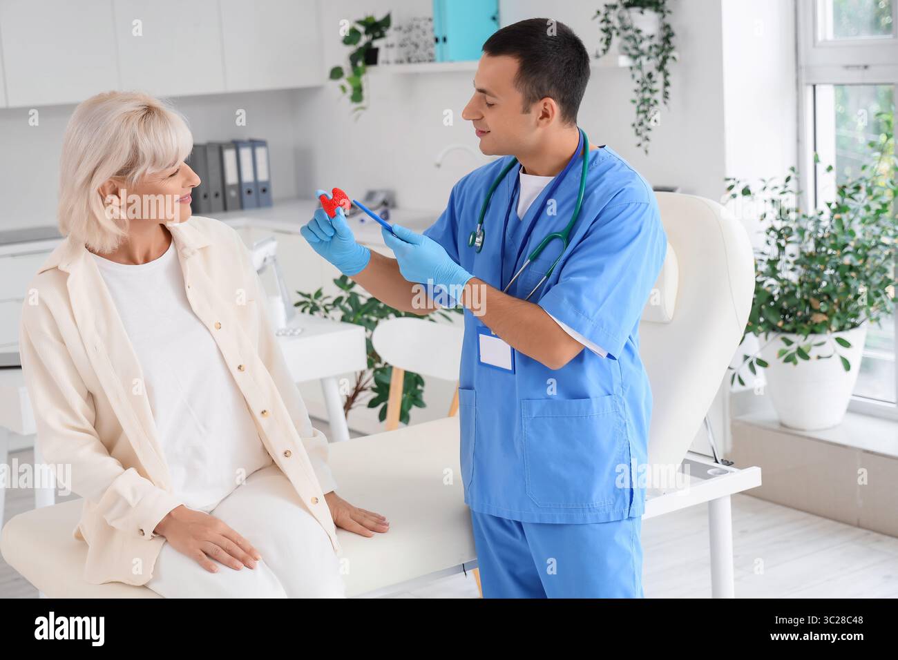 Male endocrinologist showing thyroid gland model to female patient in ...