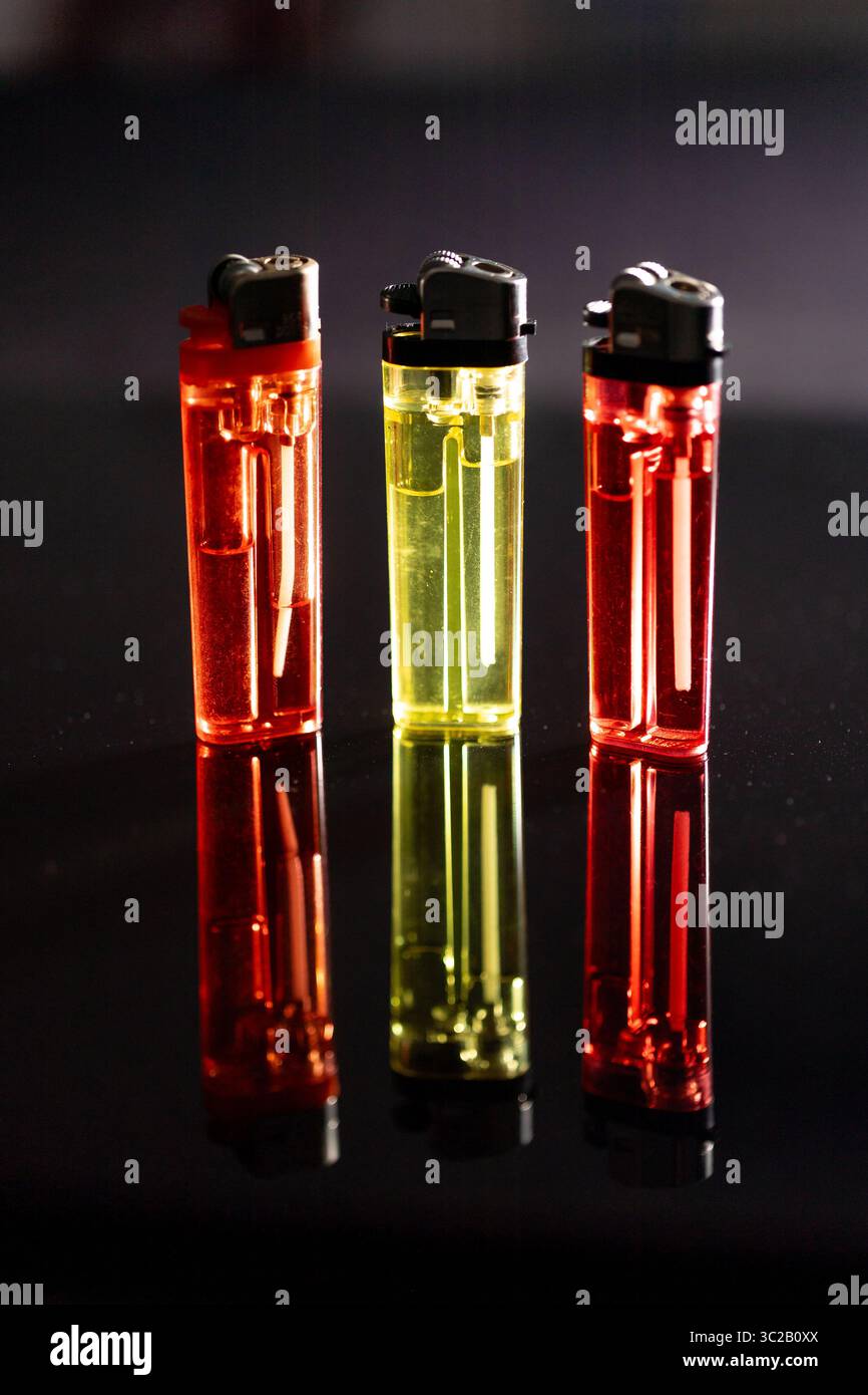 Three disposable lighters in red, yellow, and red are standing upright ...
