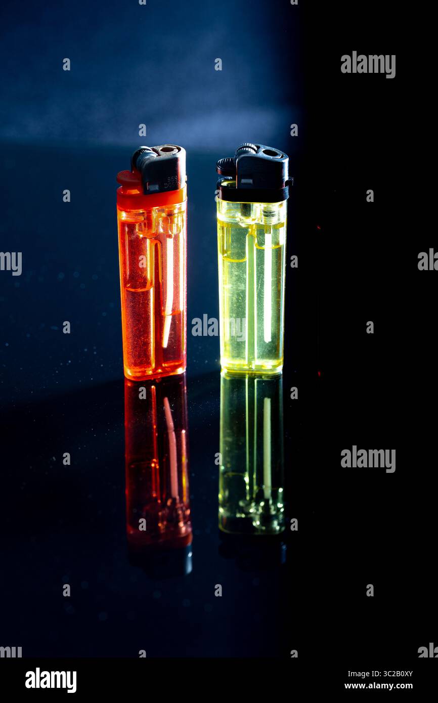 Two disposable lighters in red and yellow are standing upright on a ...