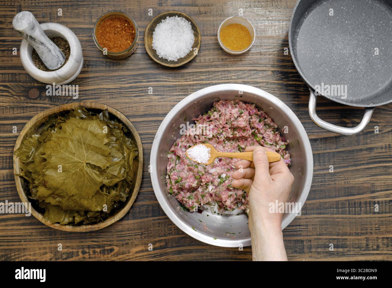 Adding sea salt into a bowl with minced lamb meat. Hands are preparing ...