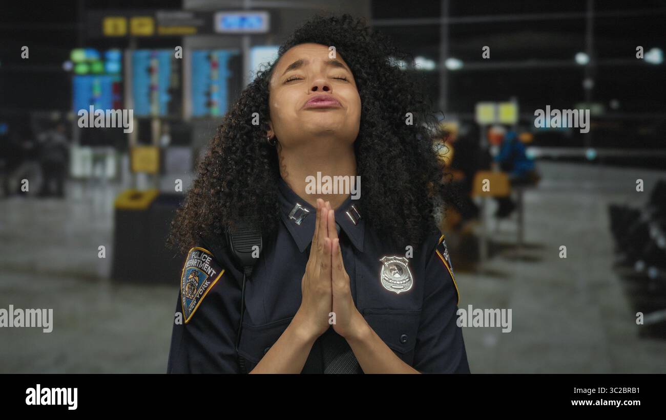 Woman police officer in uniform praying emotionally indoors at airport ...