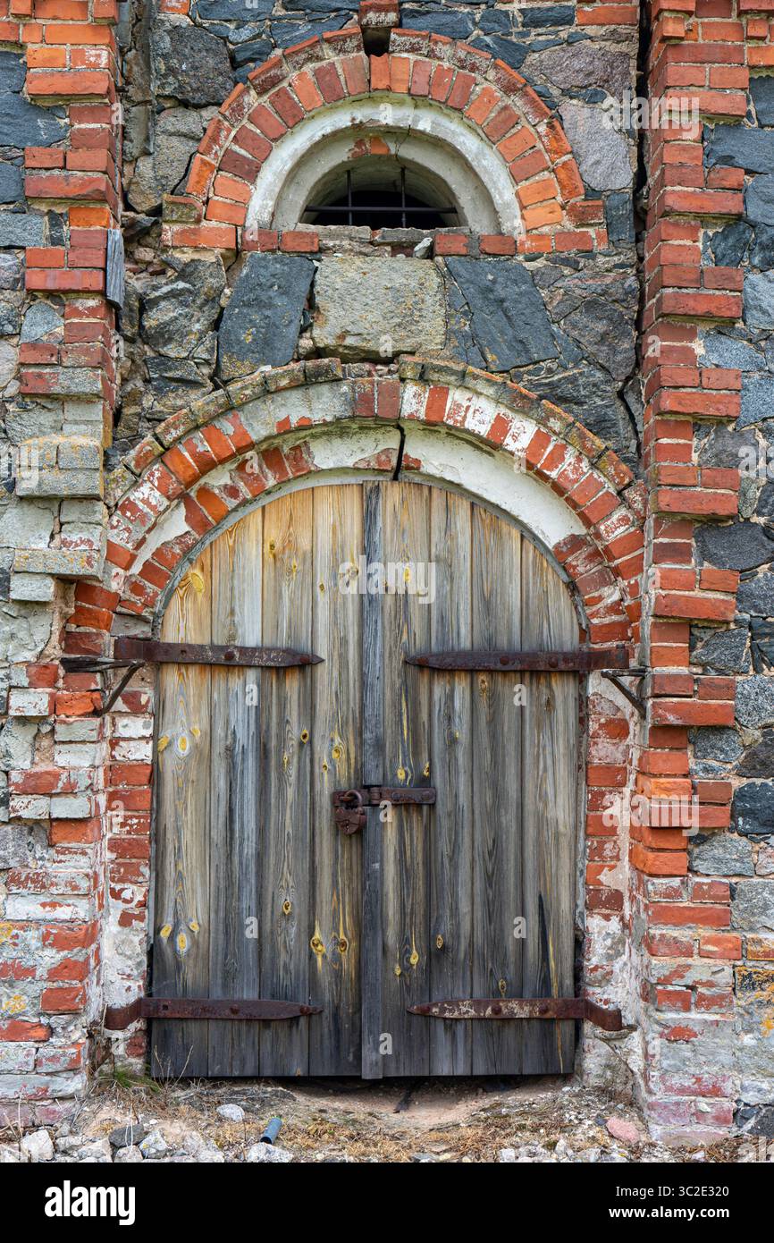 Weathered wooden doors set within an arched brick and stone facade, featuring a small arched ...