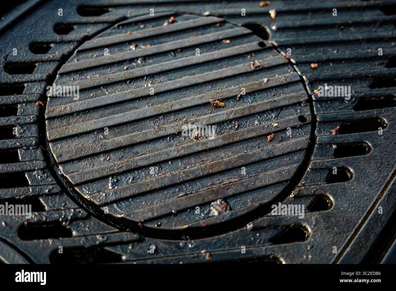 A black grill grate with a hole in the middle. The grate is dirty and ...