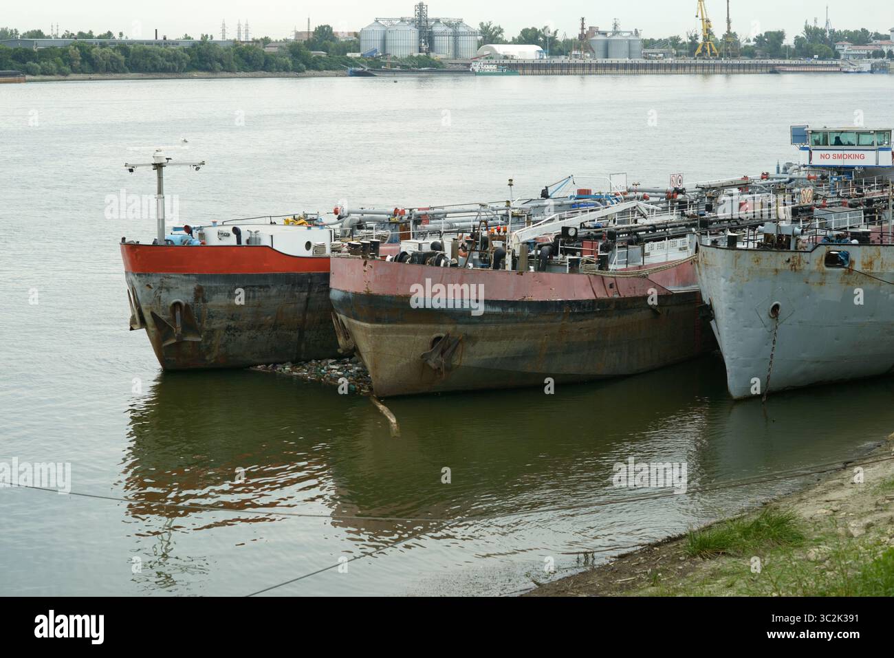 Rusty cargo barges moored on the Danube River show floating trash ...