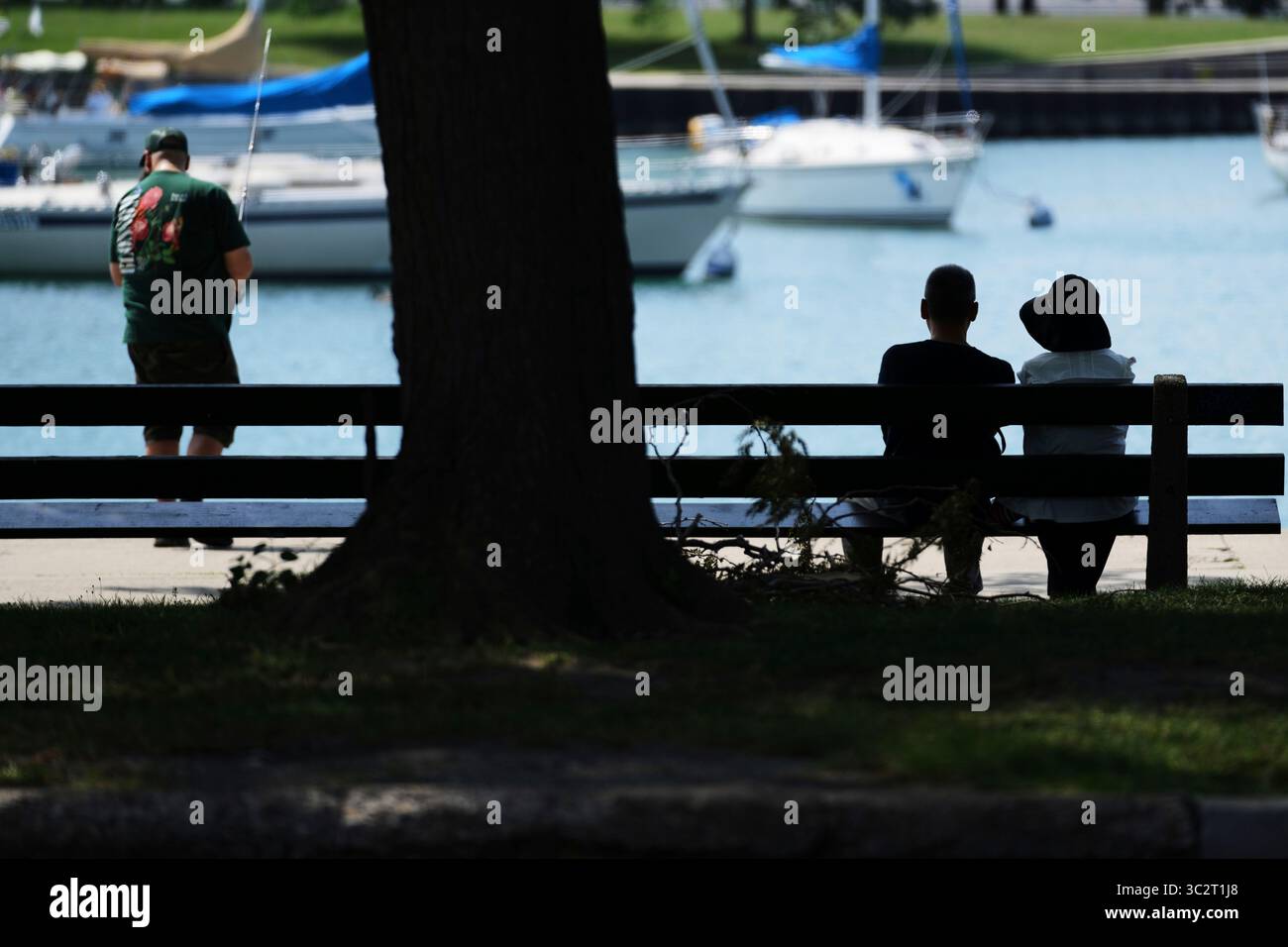 People sit down under the shade as they cool off during hot weather in ...