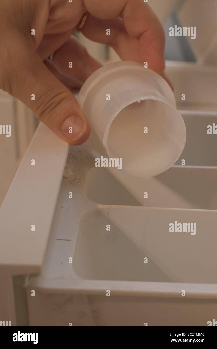 Female hand pouring fabric softener from cap into washing machine ...