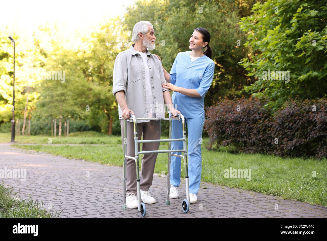 Smiling nurse supporting elderly man who using walking frame outdoors ...