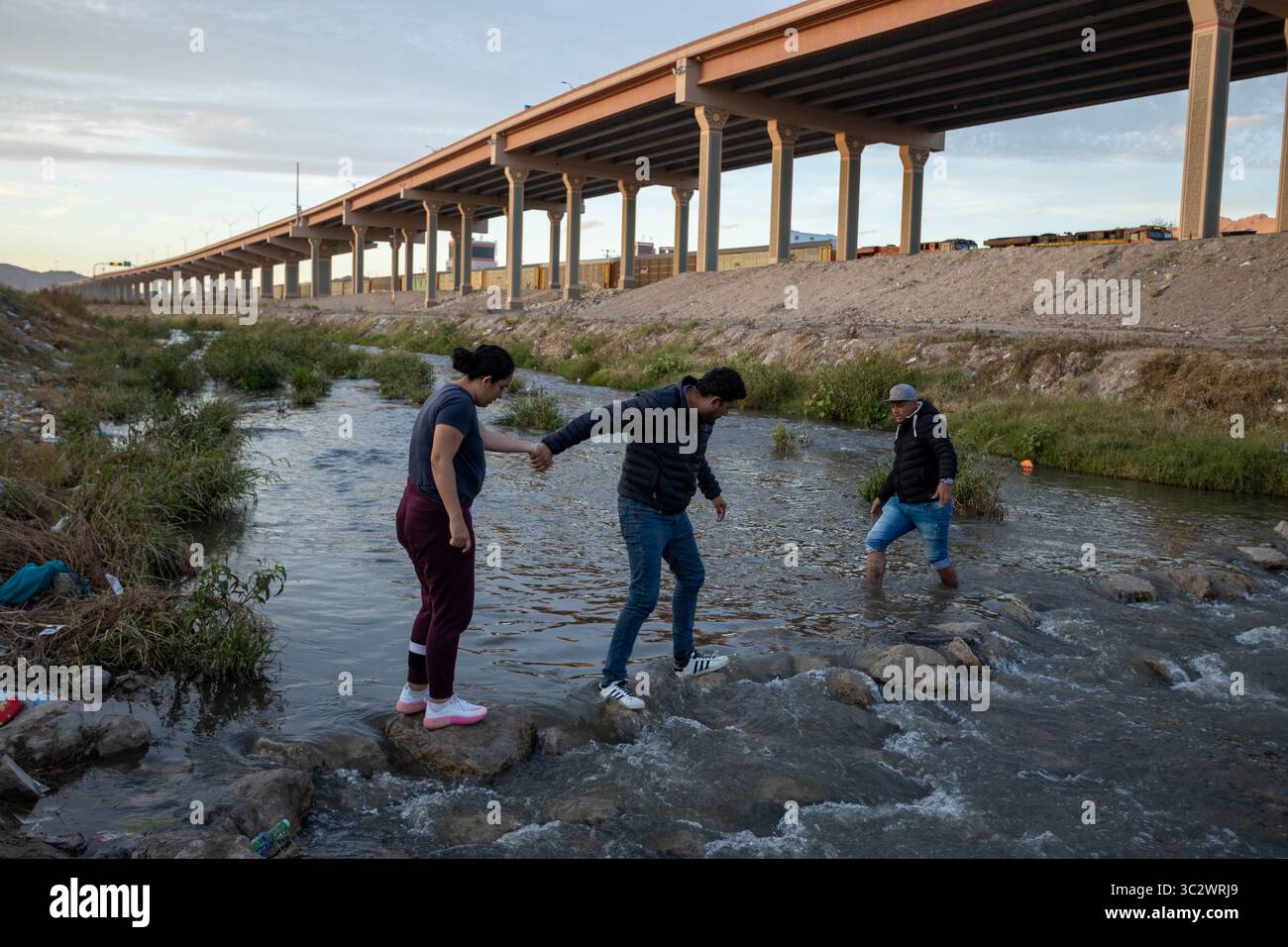Migrants cross a stream under a bridge at twilight near Ciudad Juarez ...