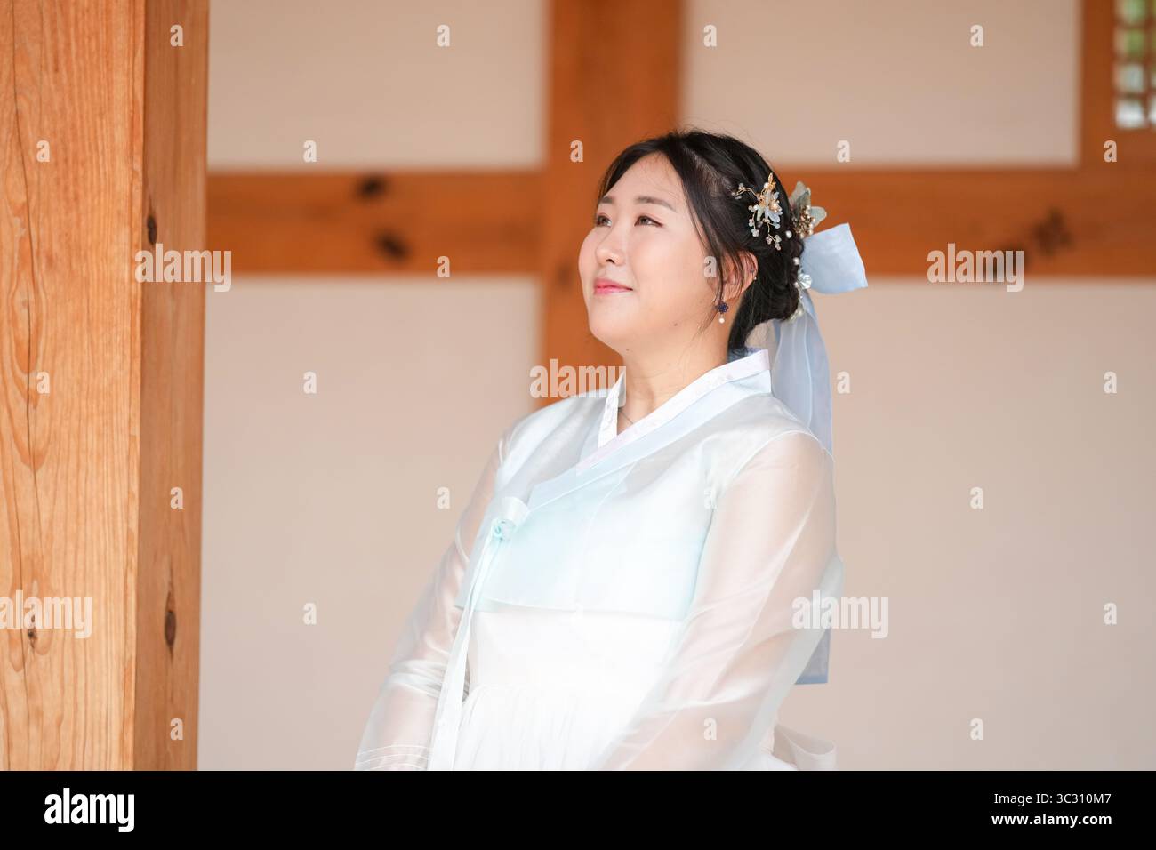 A Korean woman in her twenties wearing a sky-blue hanbok peeks from the ...