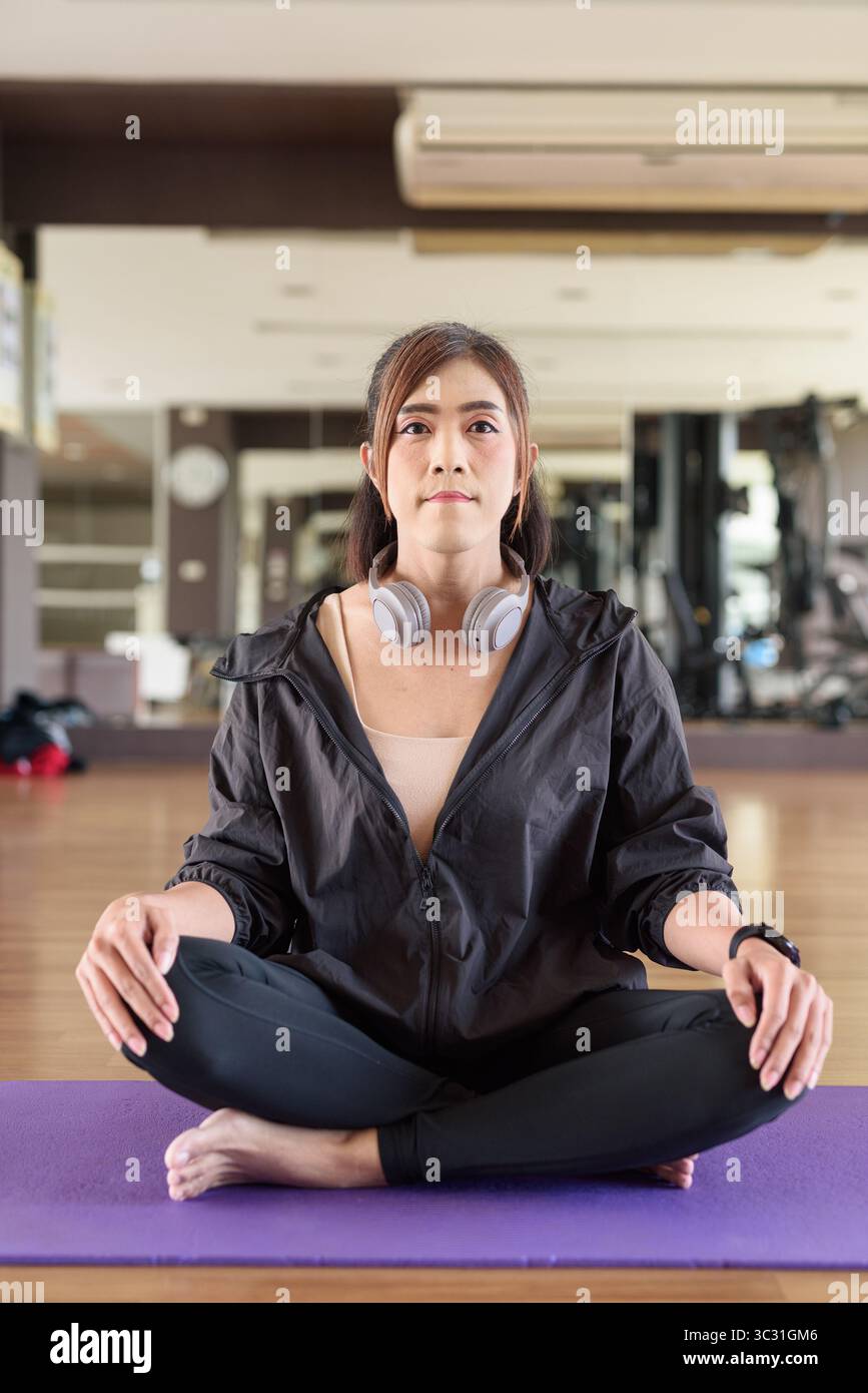 Transgender woman in 40s practicing yoga in a gym fitness environment ...
