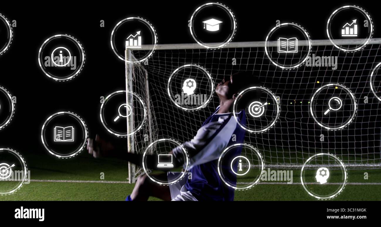 Diving soccer player wearing blue kit saving goal on night pitch, with ...