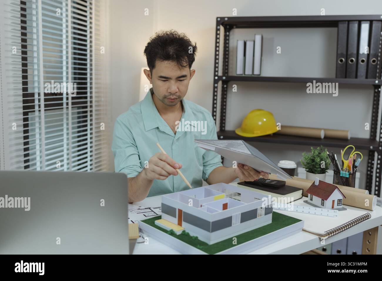 Asian male architect is analyzing a modern house model while holding ...