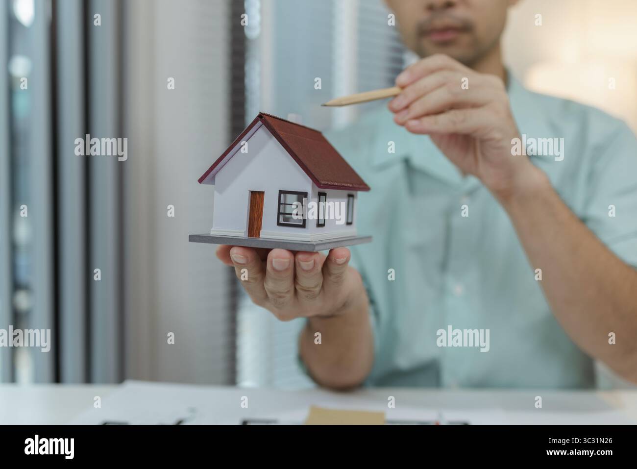 A man holding a small house model with one hand while pointing at the ...