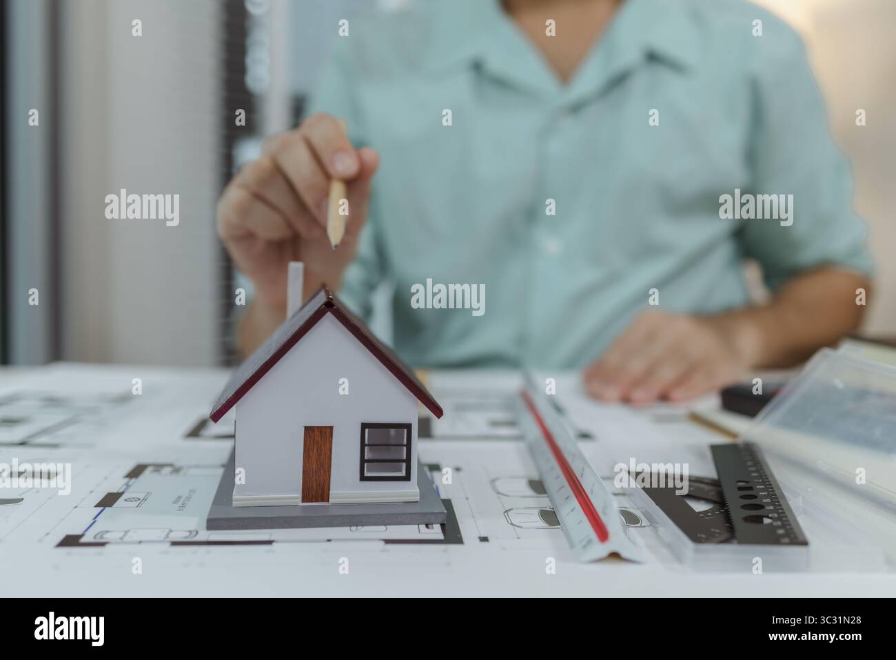 An architect pointing at a house model placed on building blueprints ...