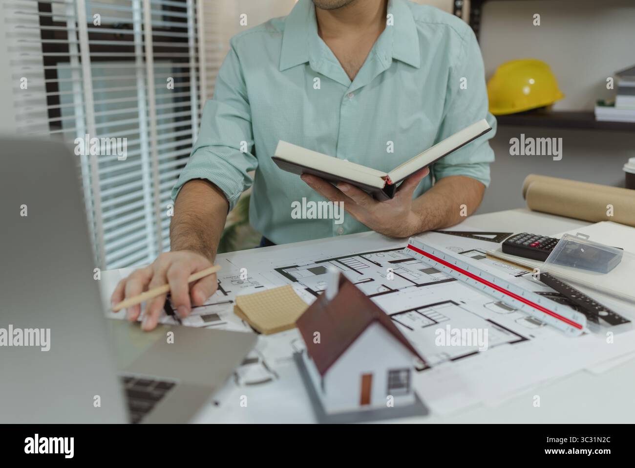 Architect working on a house plan using a pencil while referencing a ...