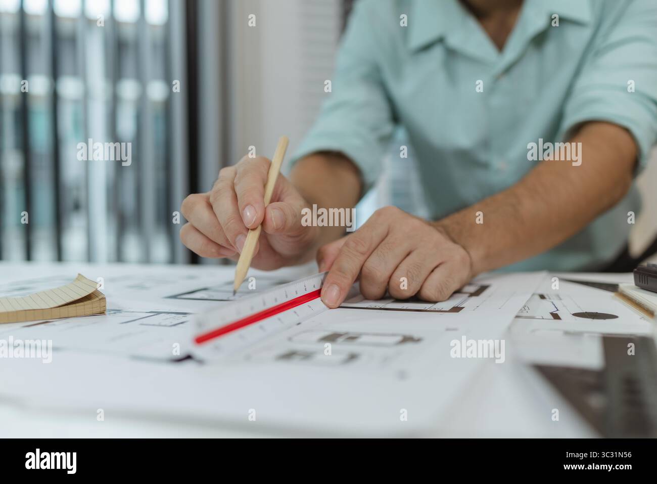 An architect using a pencil and a scale ruler to measure house floor ...