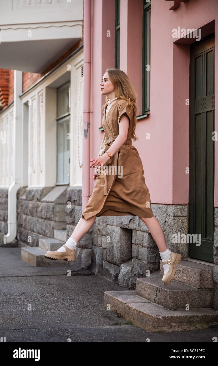 Young woman in linen dress jumping off urban stone stairs in city ...