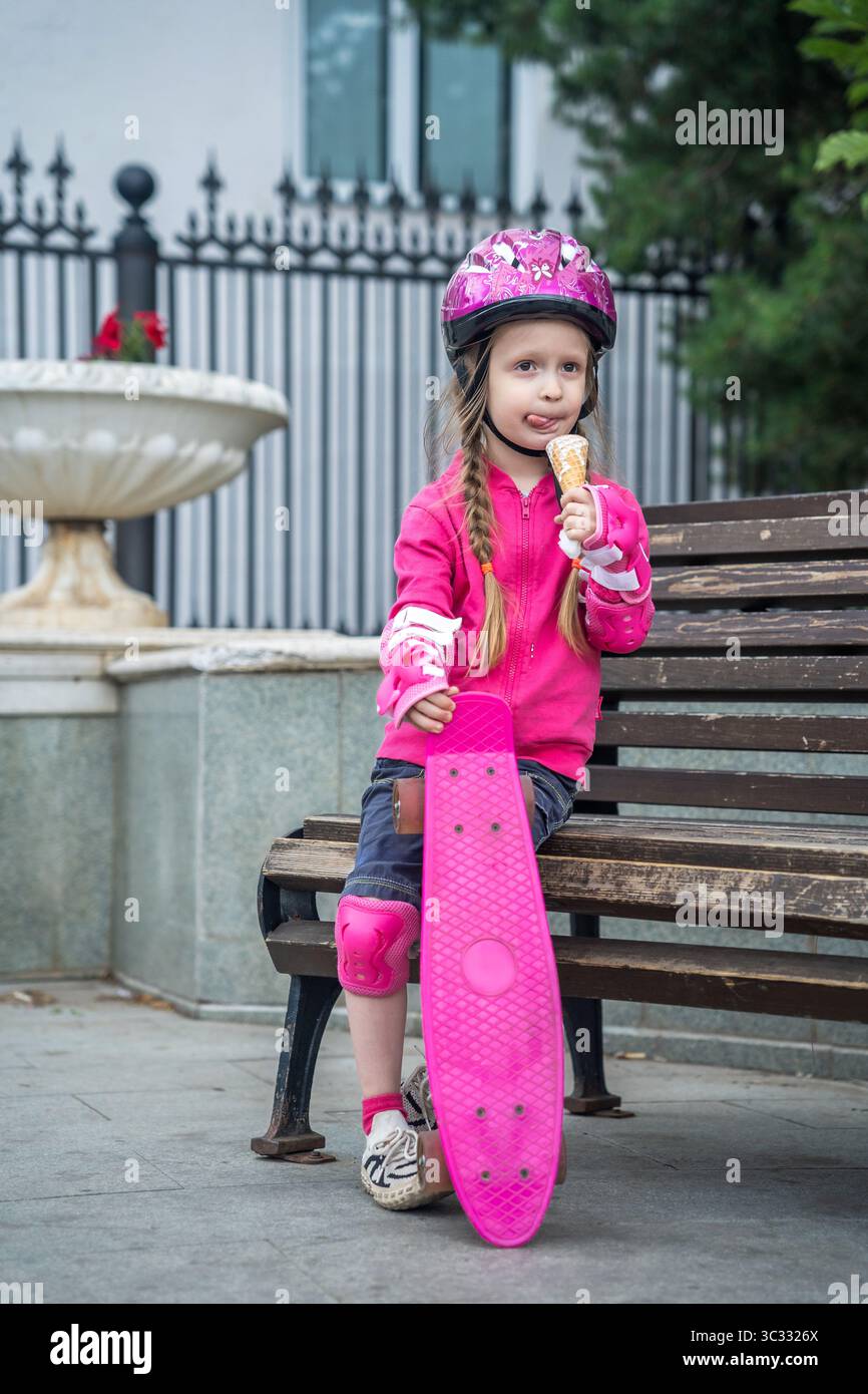 Skater girl with ice cream sitting on bench with her pink skateboard ...