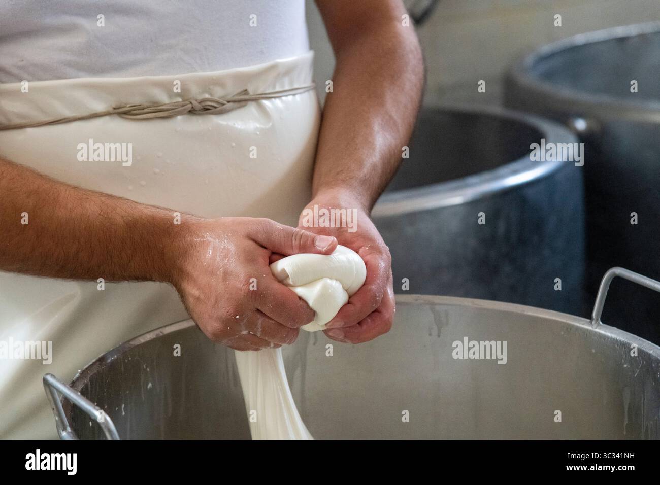 Close up of a person kneeding strings of mozzarella cheese above a ...