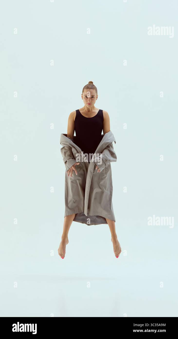 Contemporary dancer floating in mid-air with focused gaze and trench ...