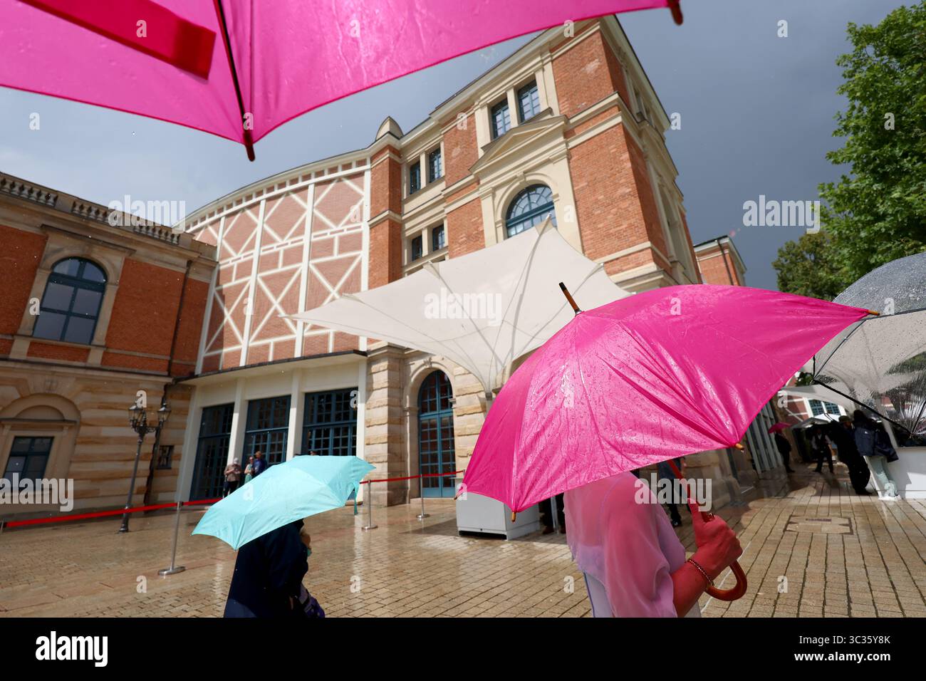 25 July 2025, Bavaria, Bayreuth: People stand with umbrellas on the ...