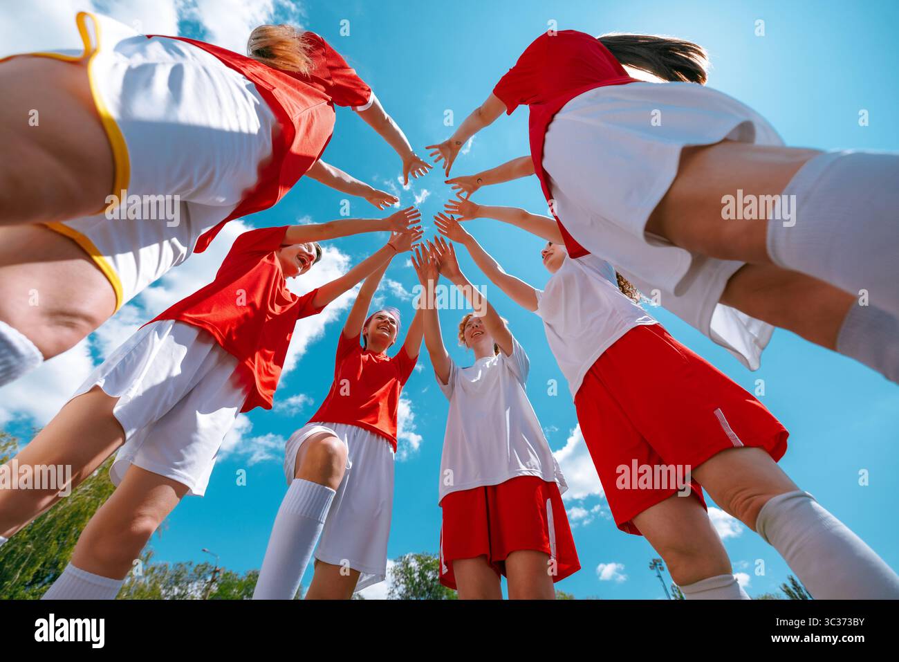 Girls football team in red and white forming team huddle with hands ...