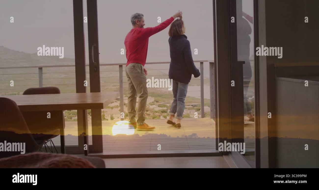 Spinning couple wearing sweaters dancing on deck outside sliding glass ...