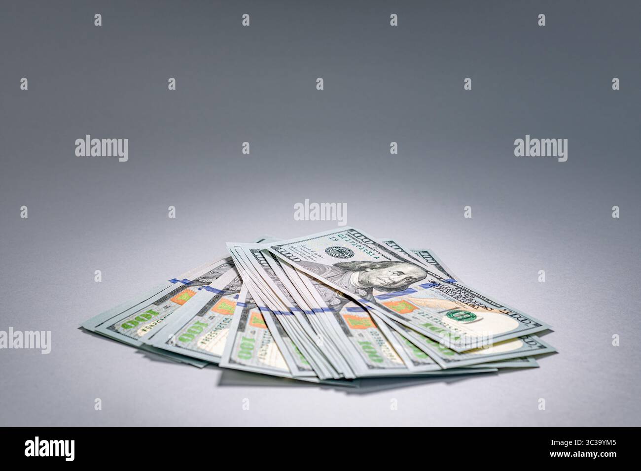 Stack of hundred dollar bills on gray background in soft spot light ...