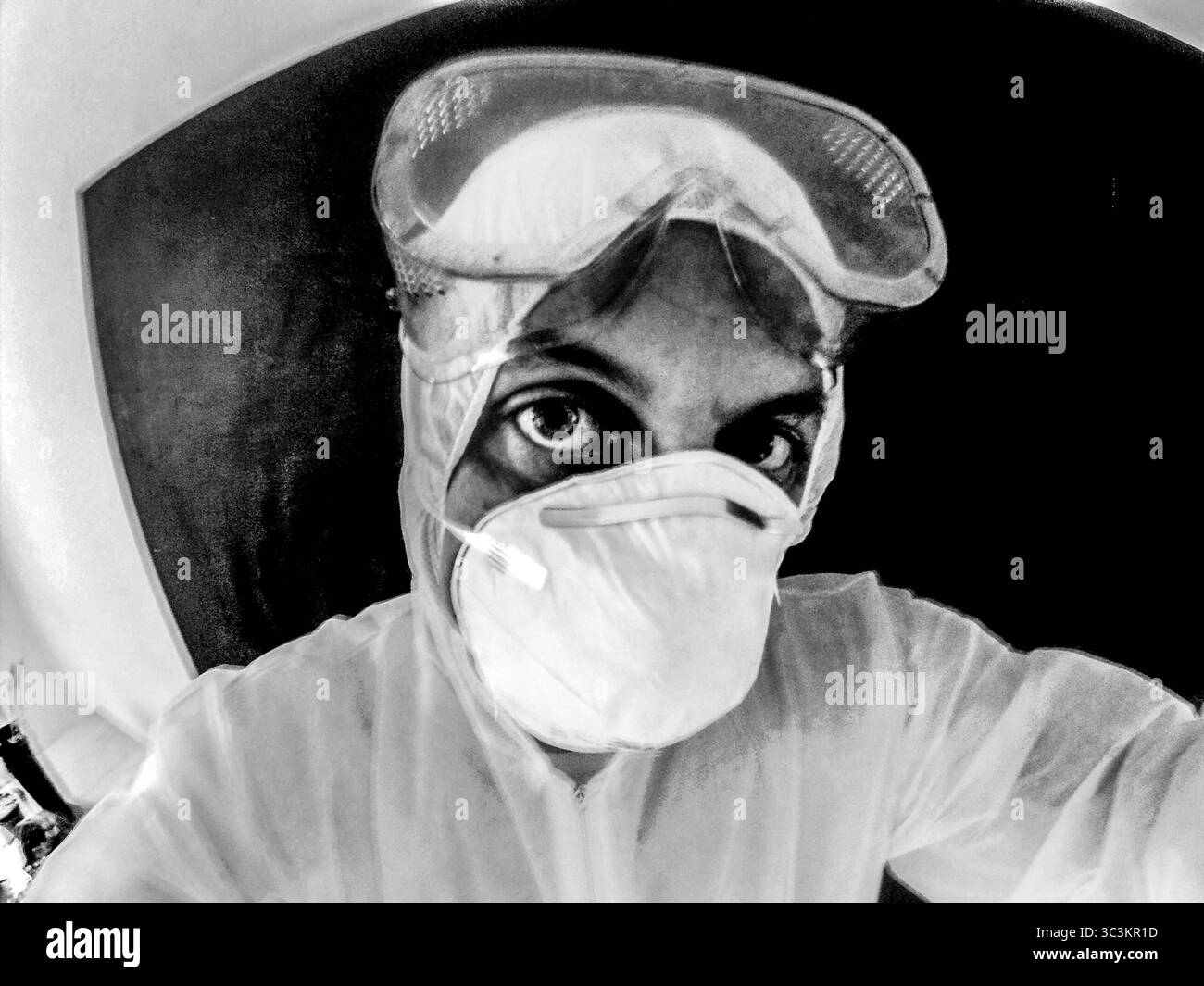 Man wearing all in one protective suit, glasses and mask looking into ...