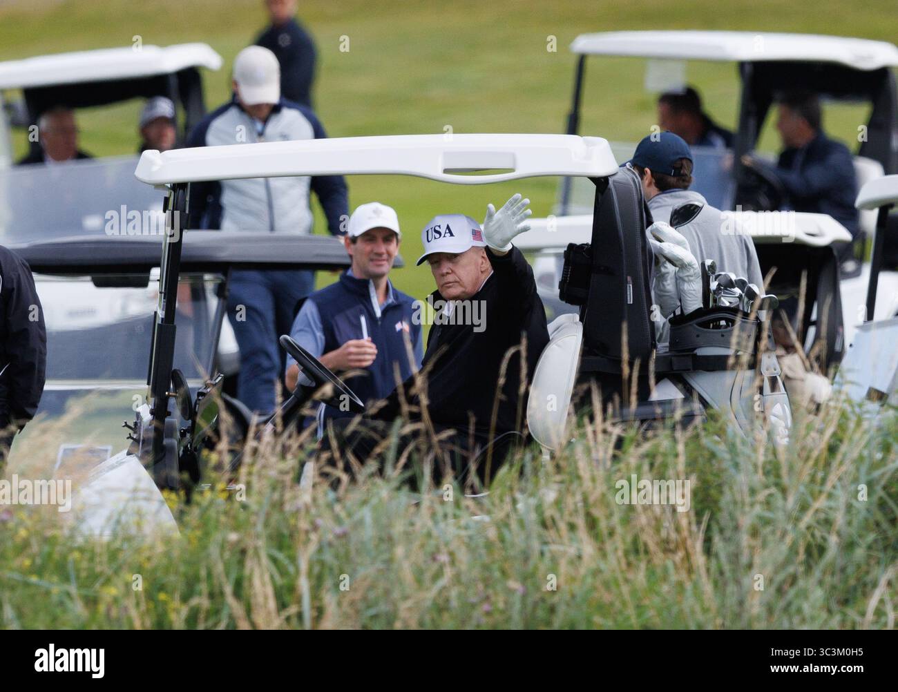 US President Donald Trump waves to reporters while in a golf cart at ...