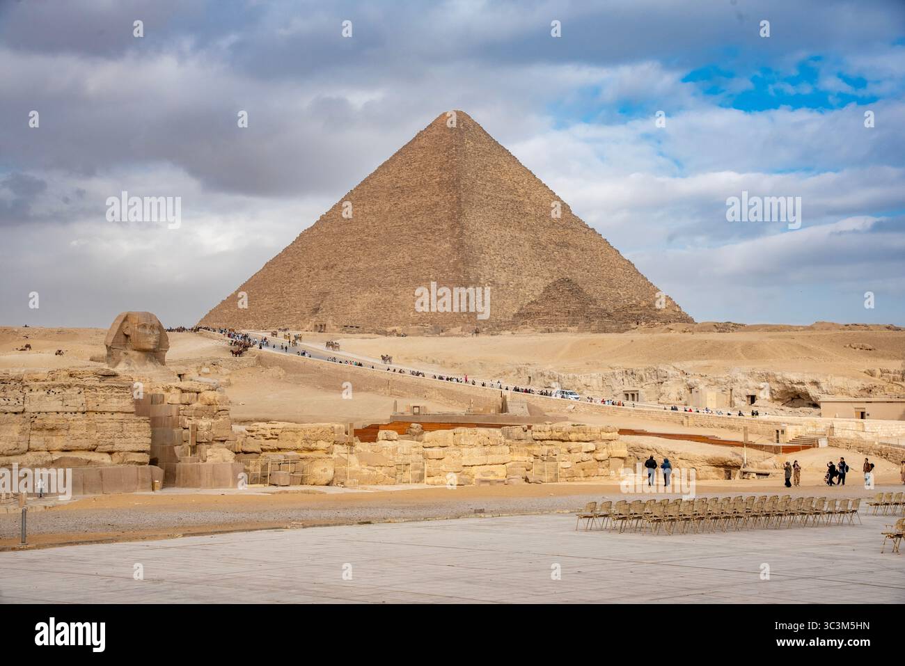Tourists walk toward the Great Pyramids of Giza with the iconic Sphinx ...