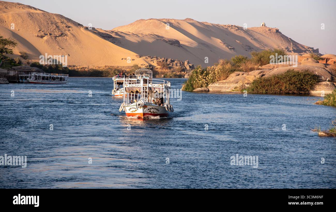 Tour boats cruising the Nile River at Aswan, Egypt, with a huge sand ...