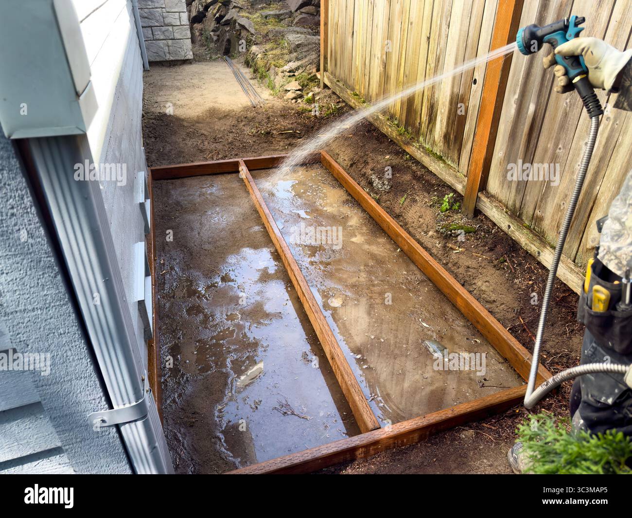 Construction worker spraying water into future concrete pad to prepare ...