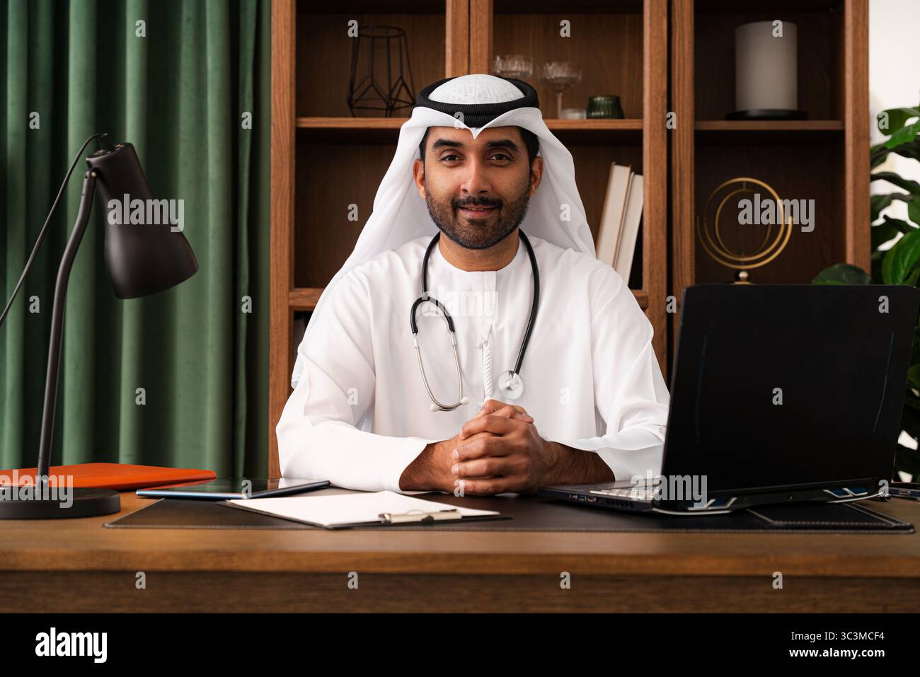 Middle-eastern doctor wearing emirati kandura working in the office ...
